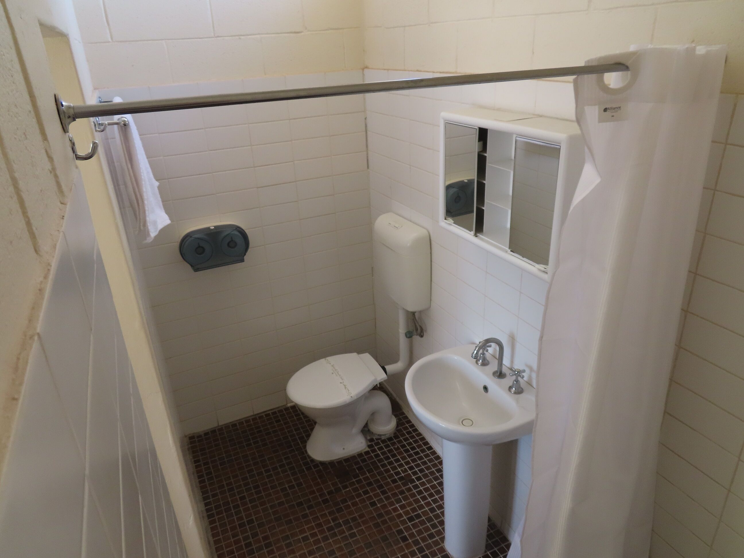 Casa de banho pequena e compacta, com sanita, lavatório e espelho sobre o lavatório.