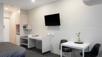 Quarto de hotel moderno com cama, escrivaninha, cadeira, televisão de tela plana na parede e uma pequena planta em vaso.