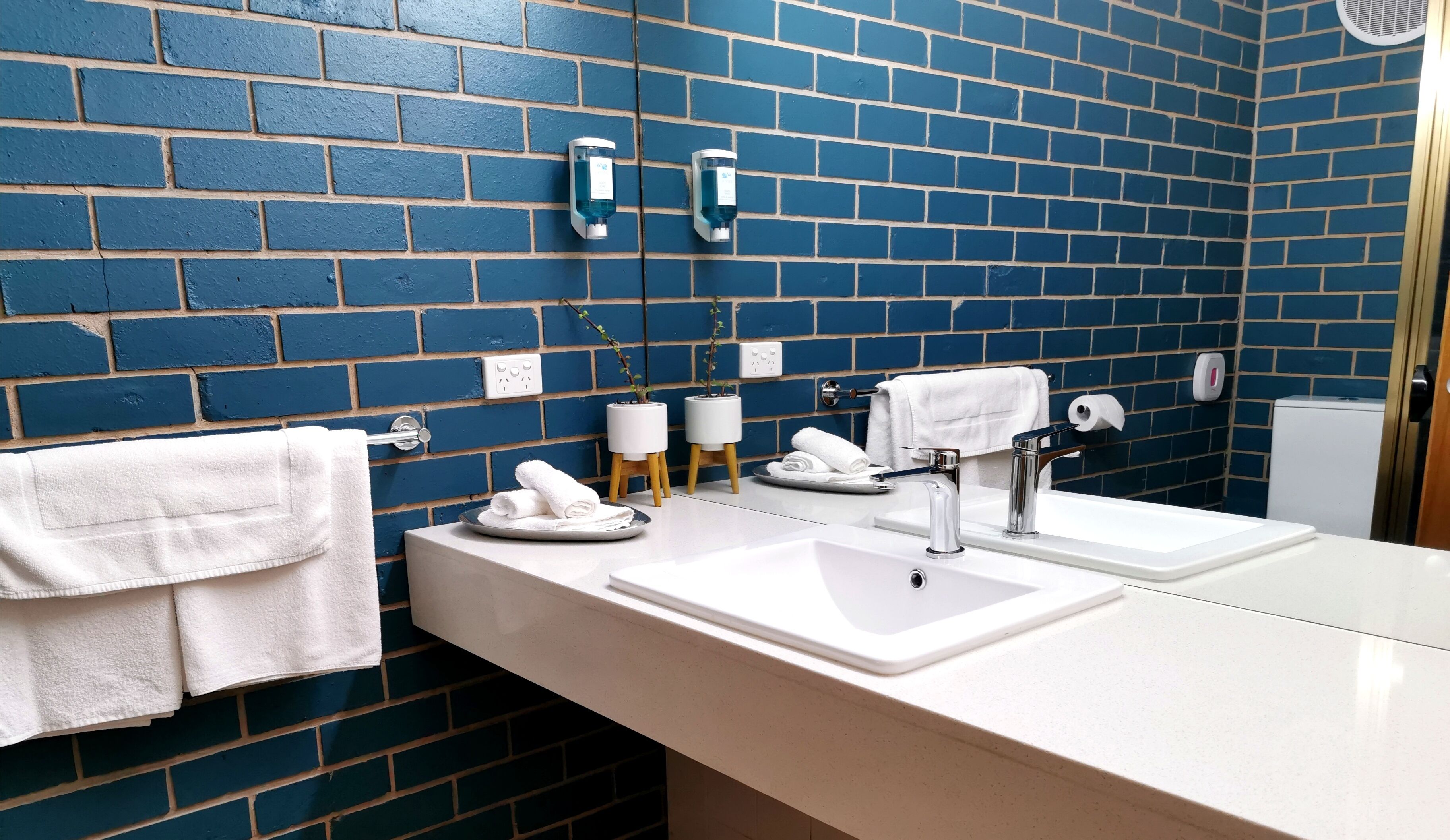 Casa de banho com duas pias, bancadas brancas e paredes de tijolo azul.