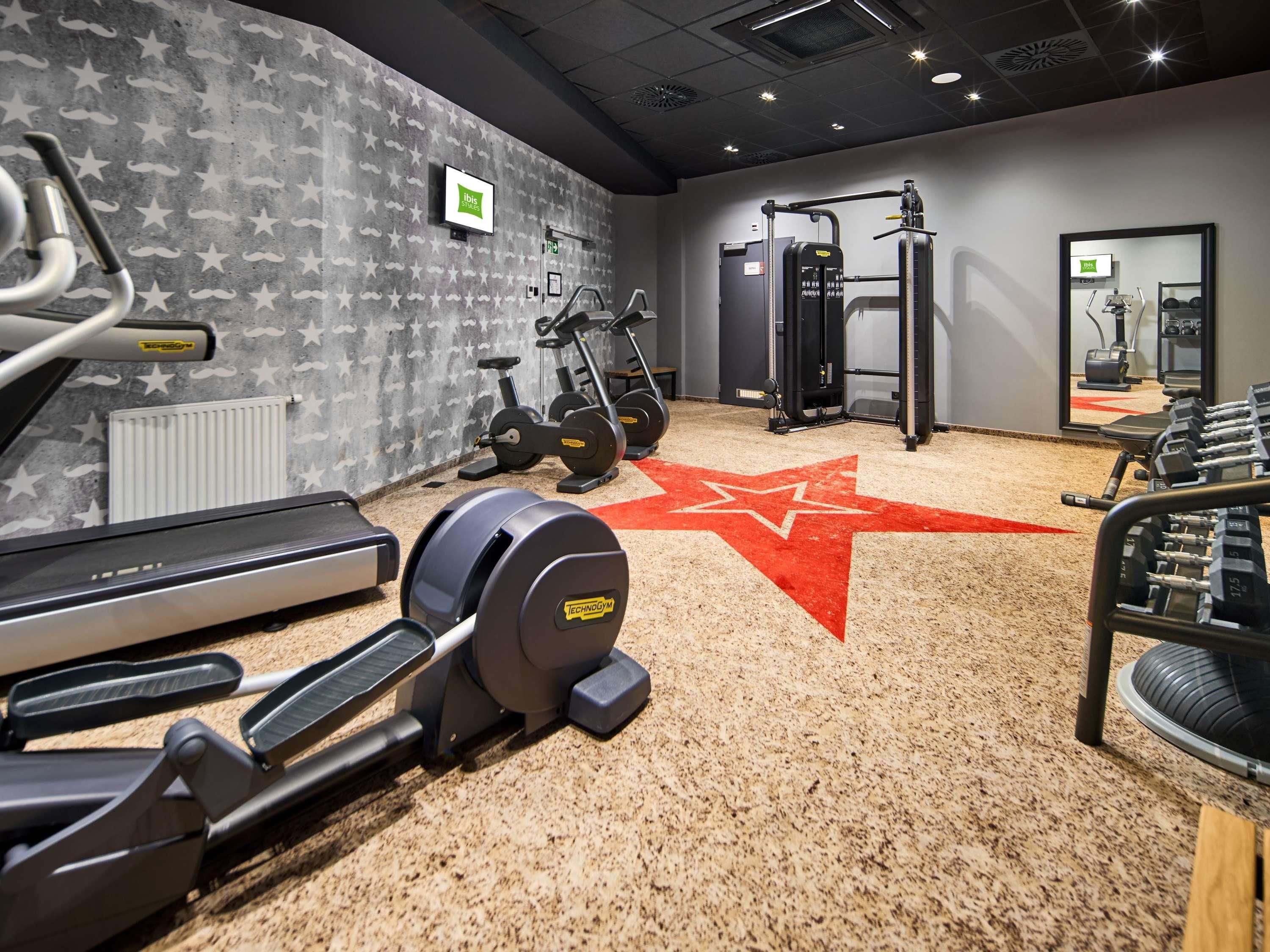 Uma academia com equipamentos de cardio, aparelhos de musculação e um tapete vermelho.