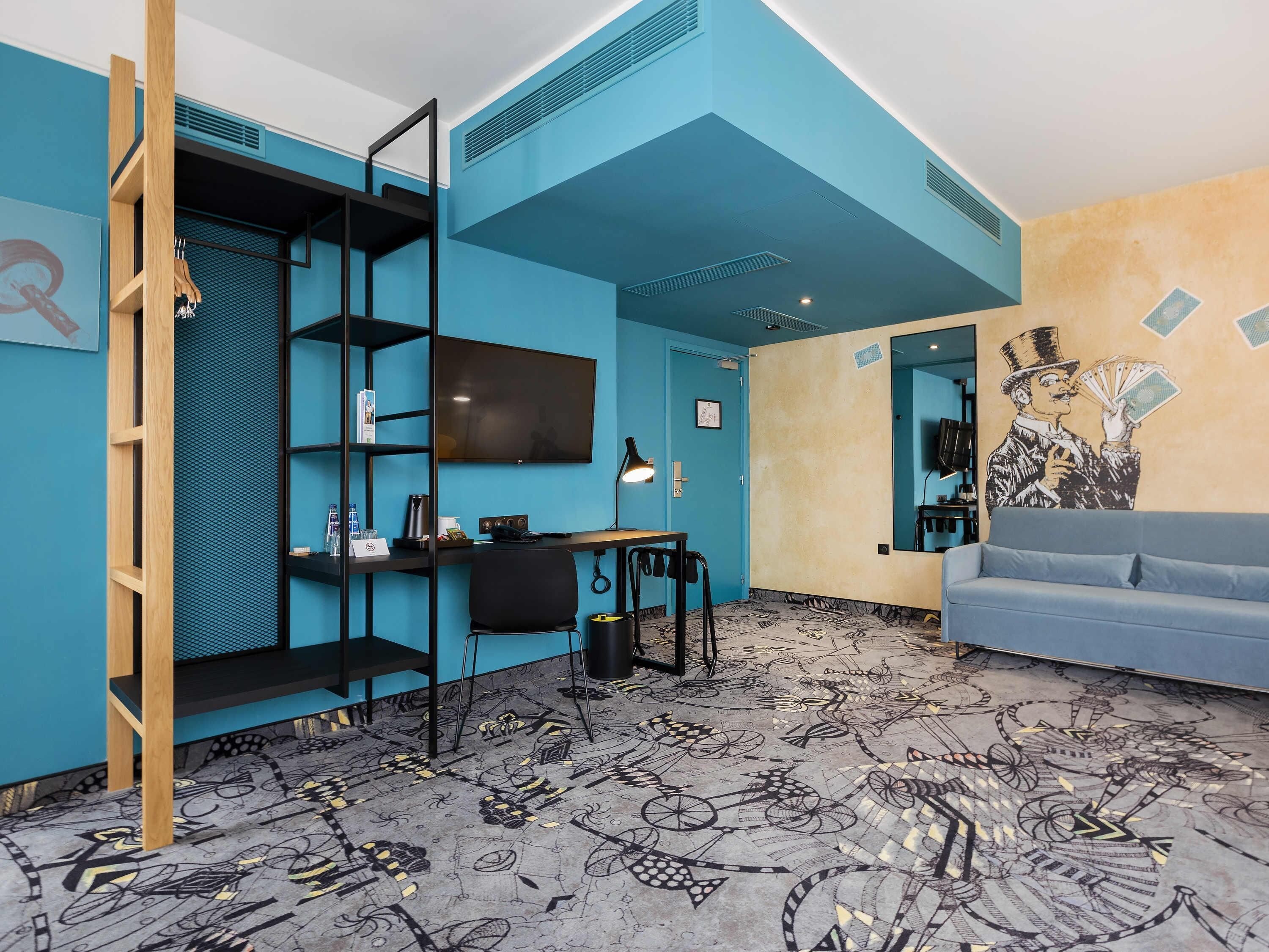 Quarto com uma parede azul de destaque, televisão montada, escrivaninha com cadeira, sofá e piso estampado.