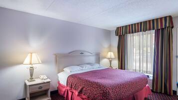 Quarto de hotel com cama, duas luminárias laterais, telefone e janela com cortinas.