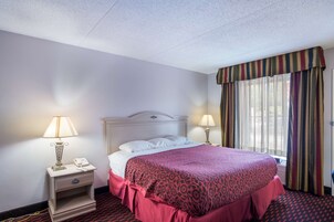 Quarto de hotel com cama, duas luminárias laterais, telefone e janela com cortinas.