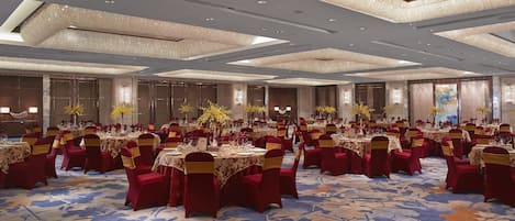 Salão de banquetes com mesas redondas, cadeiras vermelhas e flores amarelas.