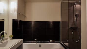 Casa de banho moderna com banheira, chuveiro com parede de vidro e toucador com espelho e lavatório.