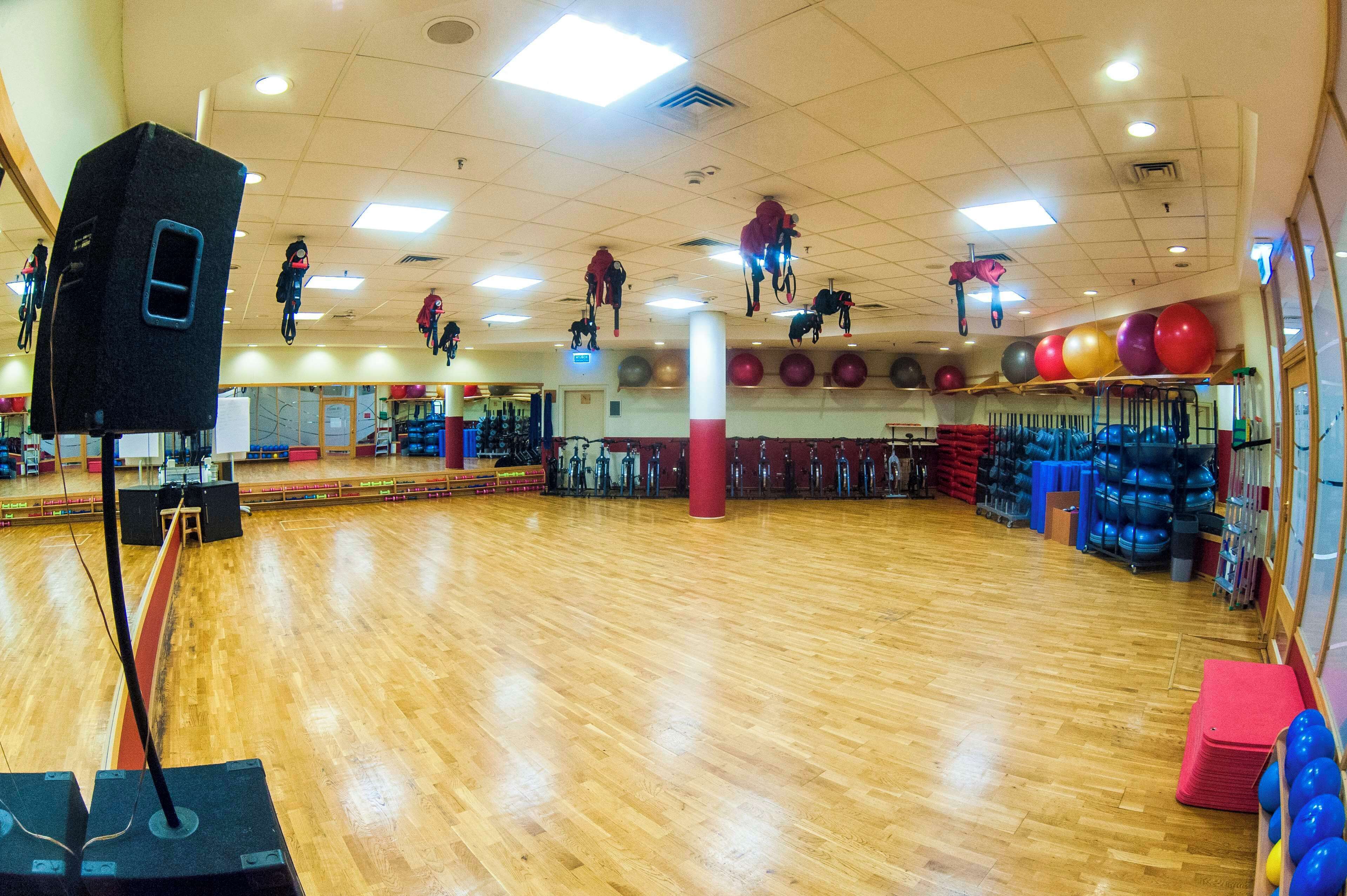 Uma academia ampla com piso de madeira, equipamentos de ginástica e diversos bolas de fitness.