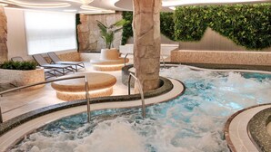 Uma área de spa com hidromassagem, cercada por espreguiçadeiras, um pilar de pedra e uma parede com plantas.