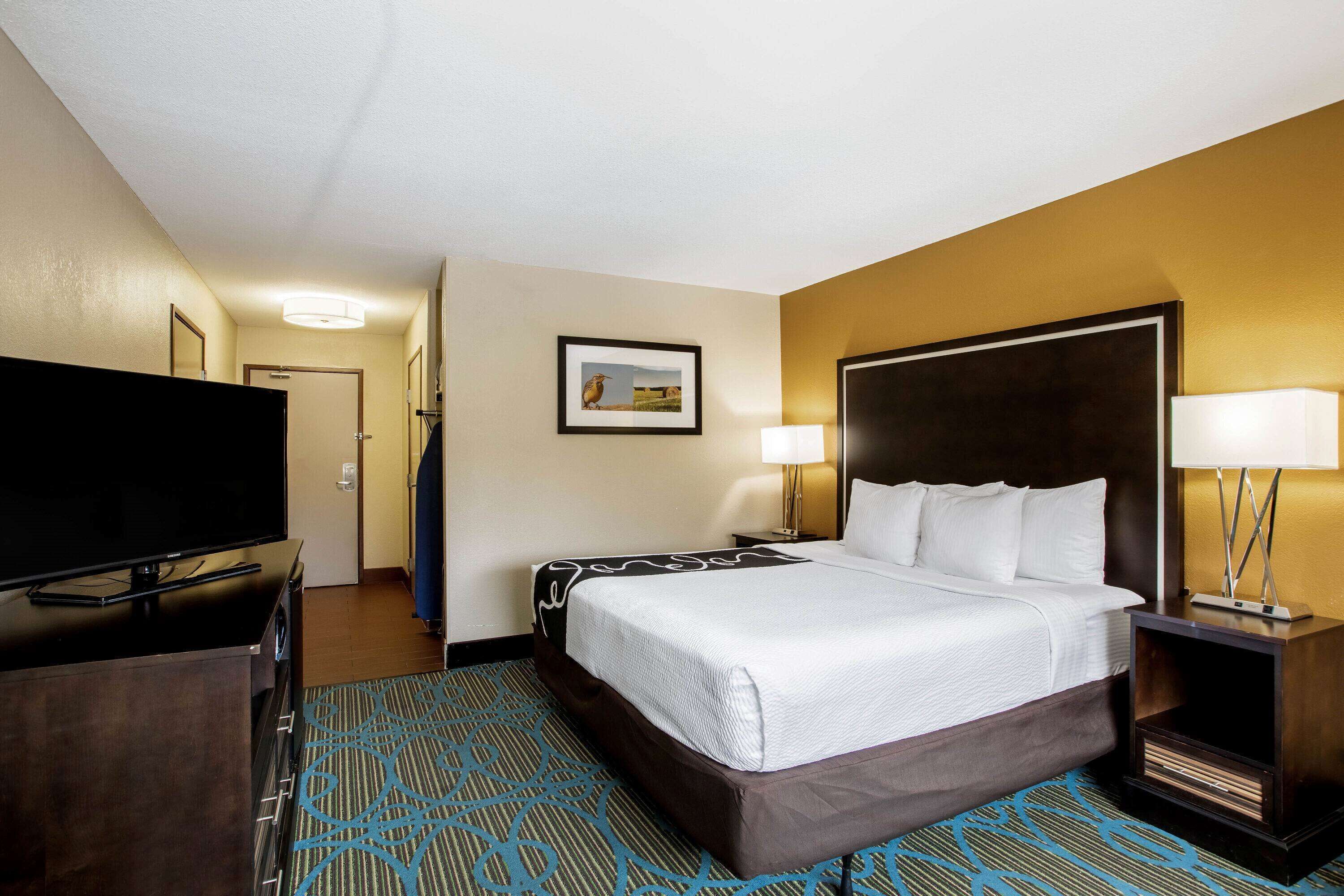 Quarto de hotel com uma cama grande, uma televisão de tela plana, uma escrivaninha e uma luminária.