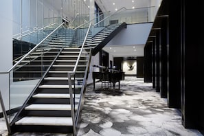 Um interior moderno com uma escadaria de vidro, um piano de cauda e um piso estampado.