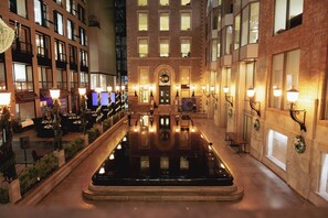 Um saguão de hotel com uma piscina refletora central, diversas áreas de refeição e uma entrada imponente com uma guirlanda.