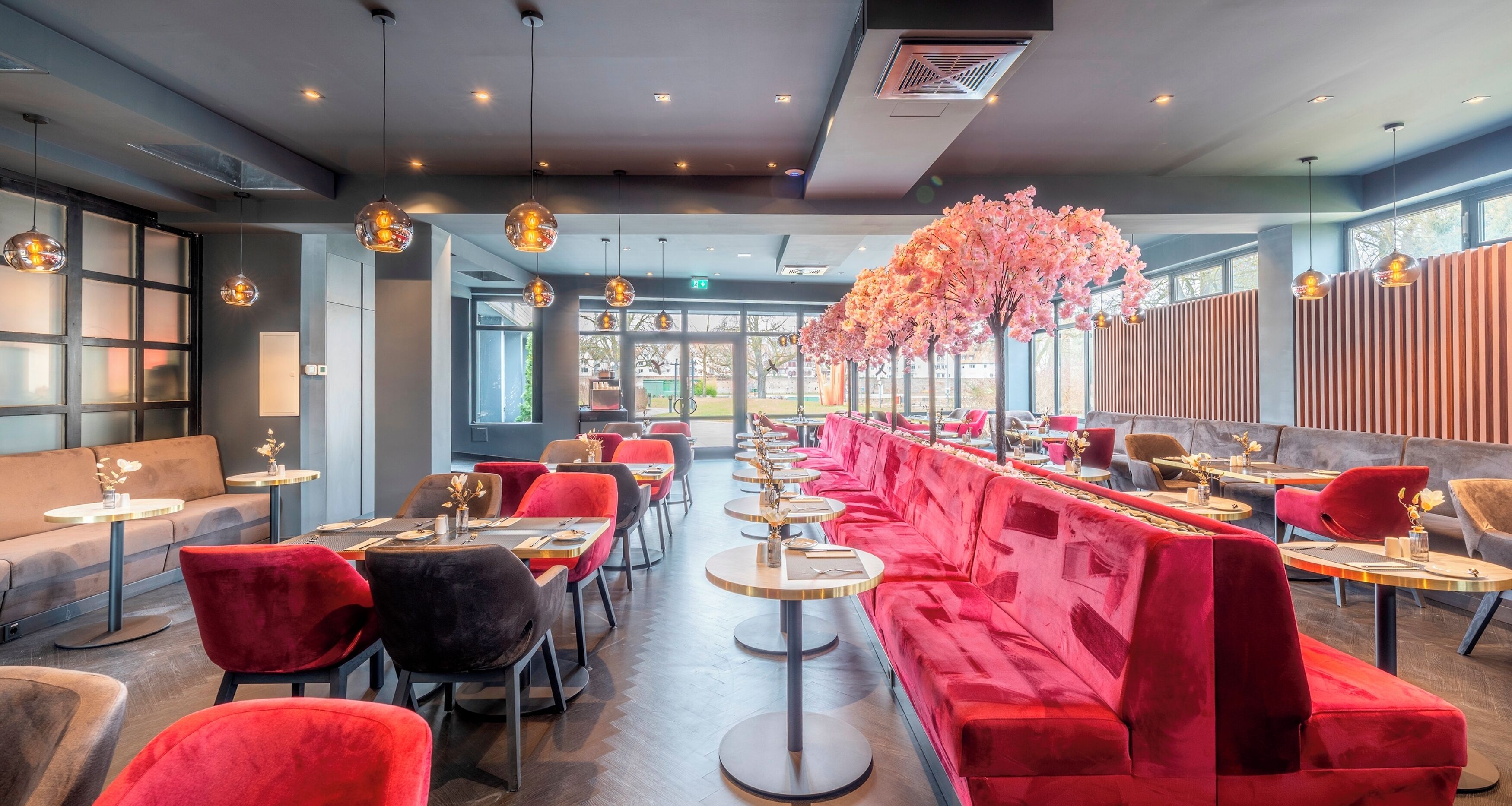 Restaurante moderno com assentos de veludo vermelho, mesas redondas e luminárias esféricas penduradas.