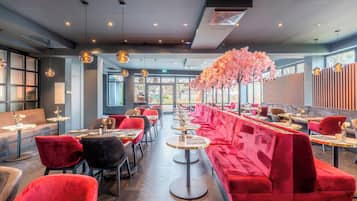Restaurante moderno com assentos de veludo vermelho, mesas redondas e luminárias esféricas penduradas.