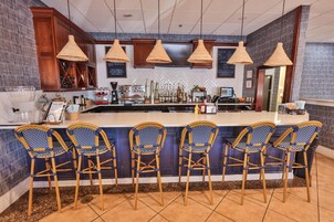 Uma área de bar com balcão, banquetas e luminárias pendentes.