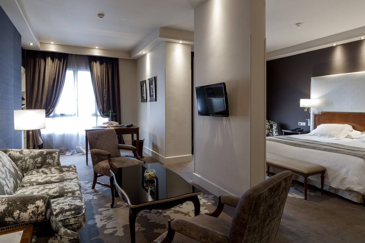 Quarto de hotel com cama, escrivaninha, cadeira, televisão e luminária.
