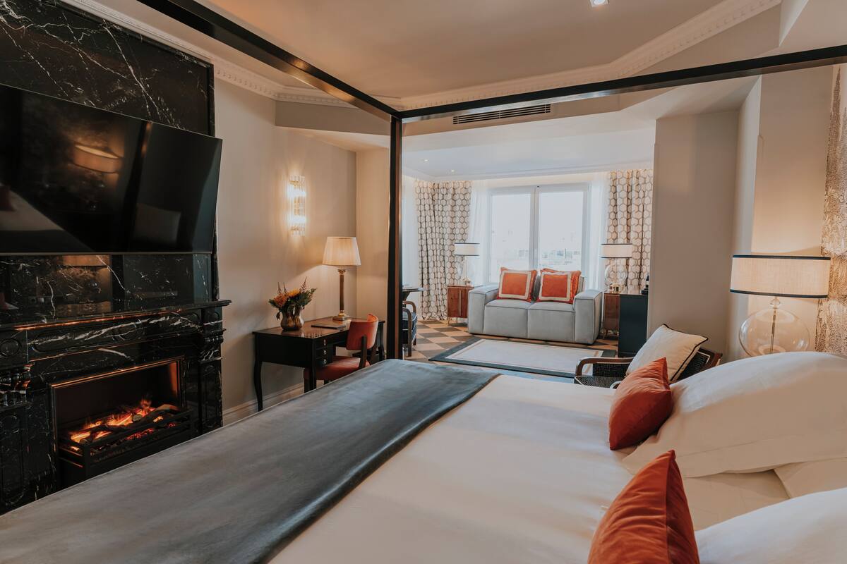 Quarto de hotel moderno com lareira, uma cama grande, um sofá e vista para a cidade.