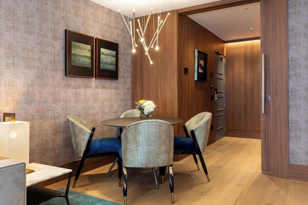 Uma sala de jantar moderna com uma mesa redonda, cadeiras estofadas em azul e um lustre decorativo.