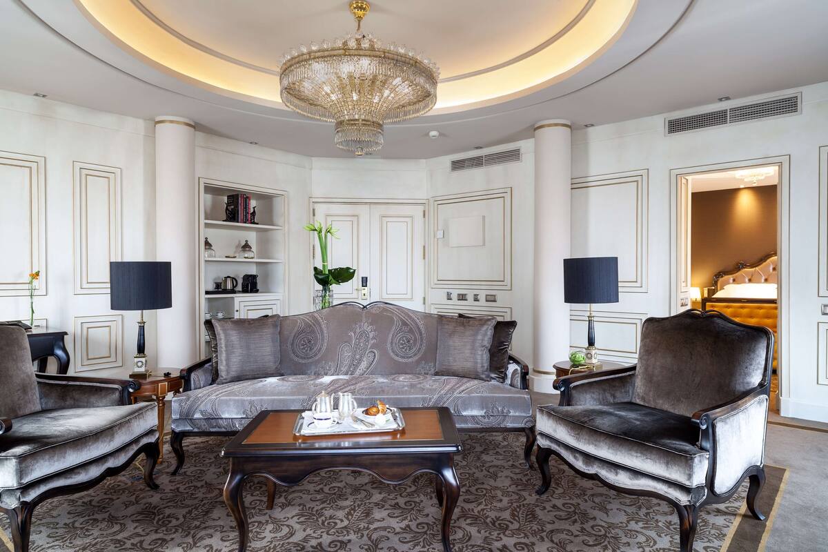Uma sala de estar luxuosa, com um imponente candelabro, móveis elegantes e uma estante de livros.