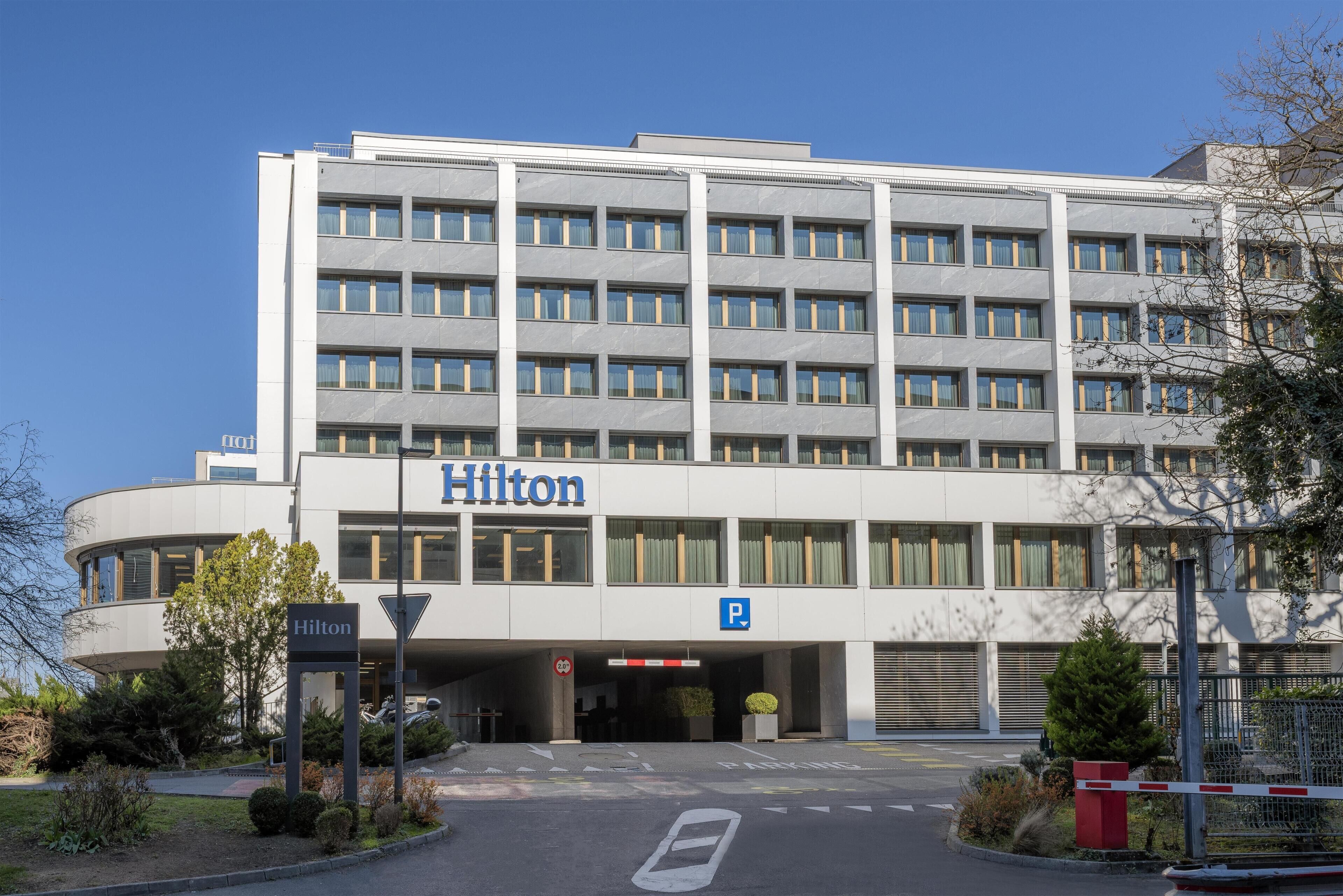 Um edifício moderno com a placa 'Hilton', uma área de estacionamento e uma entrada com portão.