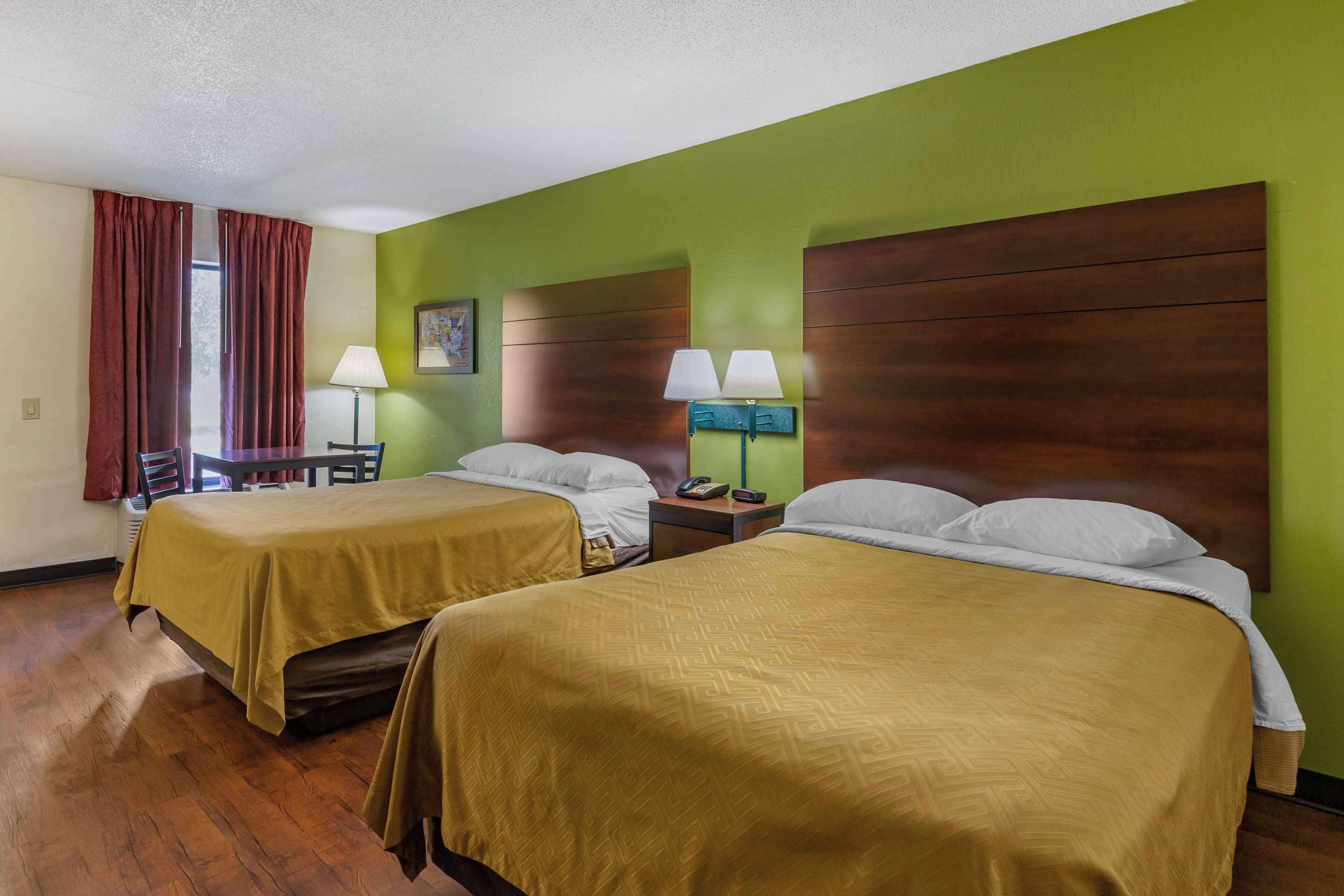 Quarto de hotel com duas camas, cabeceiras de madeira, uma escrivaninha com cadeira, abajur e telefone.