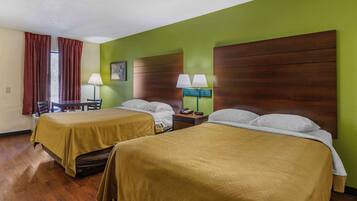 Quarto de hotel com duas camas, cabeceiras de madeira, uma escrivaninha com cadeira, abajur e telefone.