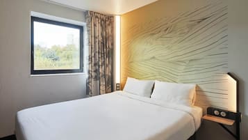 Quarto de hotel com uma cama grande, janela com cortinas, luminária na parede e mesa de cabeceira com abajur.