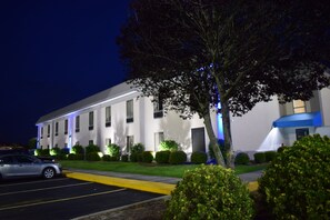 Um edifício moderno com um estacionamento e uma árvore ao primeiro plano.