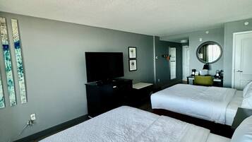 Quarto de hotel com duas camas, televisão de tela plana, escrivaninha, espelho e obras de arte nas paredes.