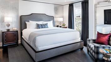 Quarto de hotel moderno com uma cama grande, uma mesa de cabeceira, uma cadeira e vista para a cidade.