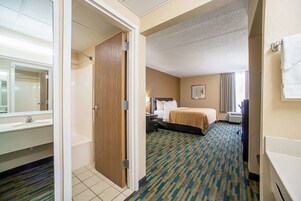 Quarto de hotel com banheiro, uma cama, mesa de cabeceira e janela.