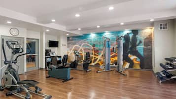Uma academia com equipamentos de cardio, aparelhos de musculação e um grande espelho.