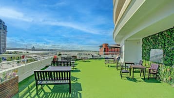Terraço no telhado com grama sintética verde, mobiliário de madeira e vista para a paisagem urbana.