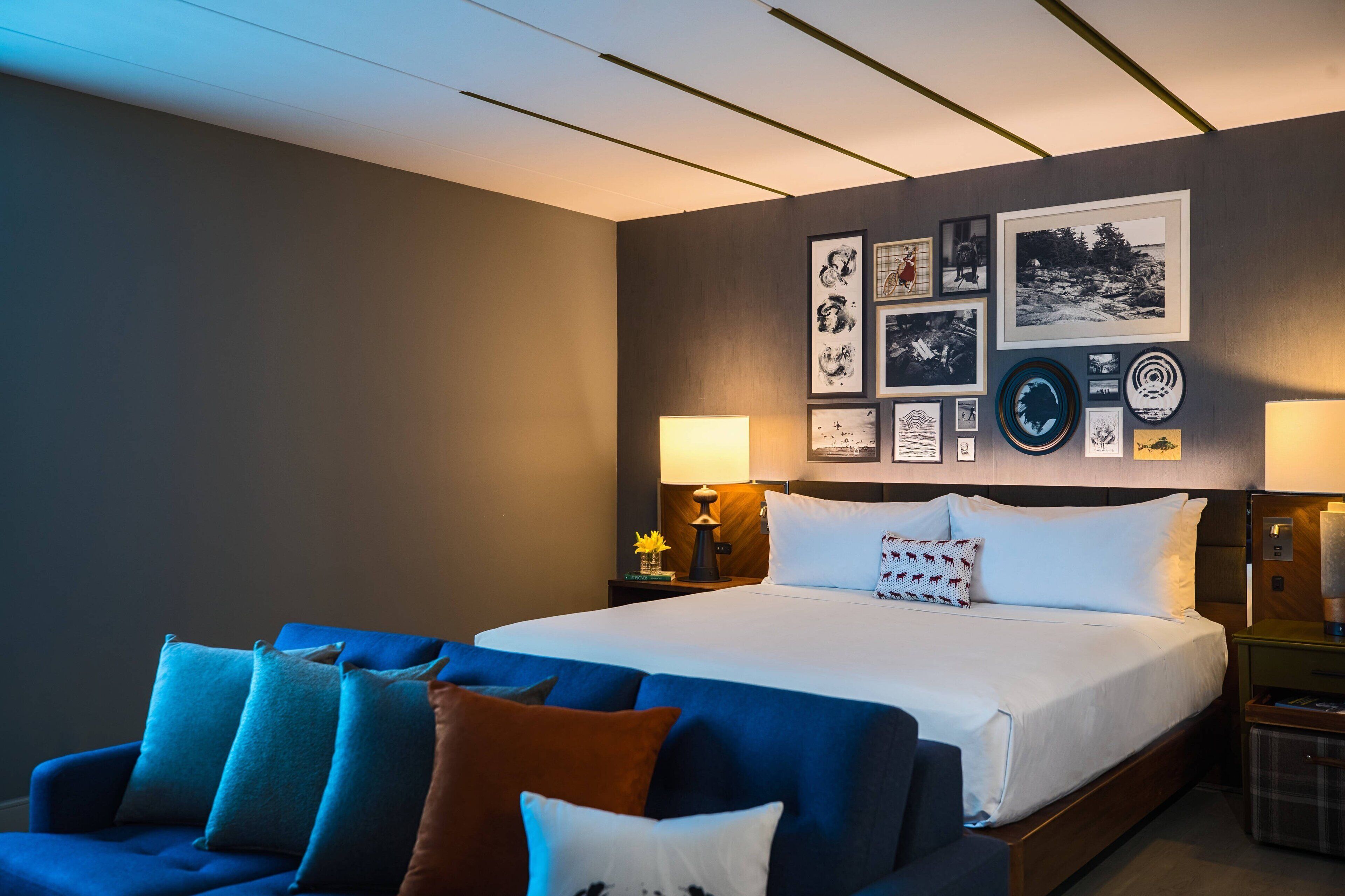 Quarto de hotel com uma cama grande, um sofá azul e uma mesa de cabeceira com abajur.