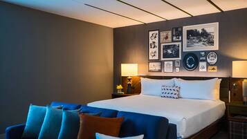 Quarto de hotel com uma cama grande, um sofá azul e uma mesa de cabeceira com abajur.