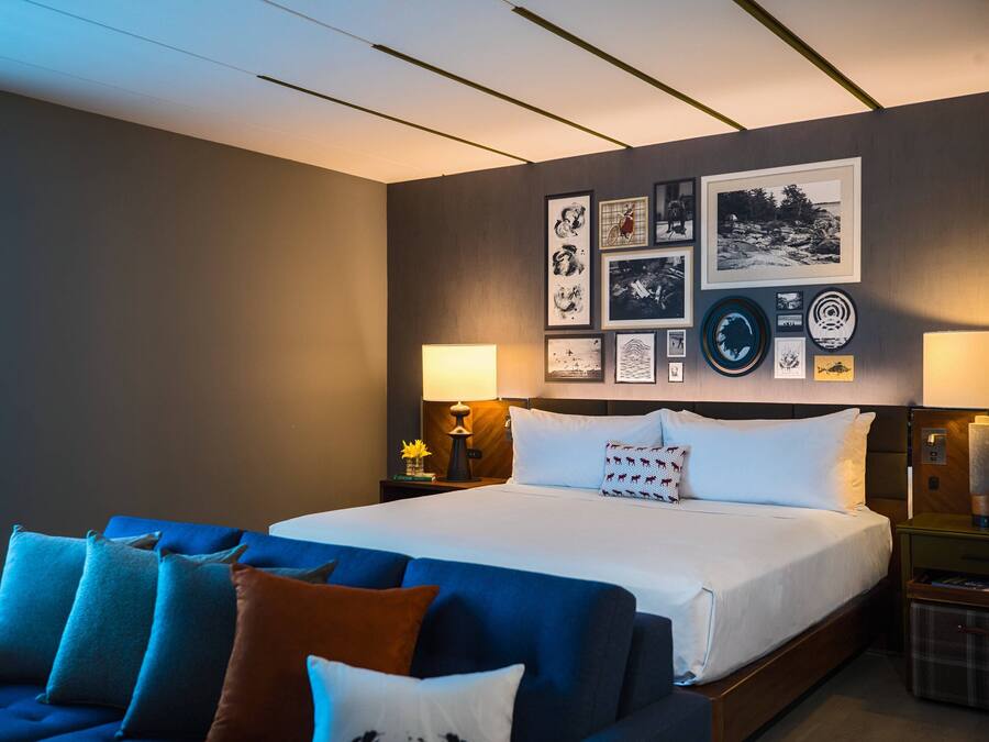 Quarto de hotel com uma cama grande, um sofá azul e uma mesa de cabeceira com abajur.