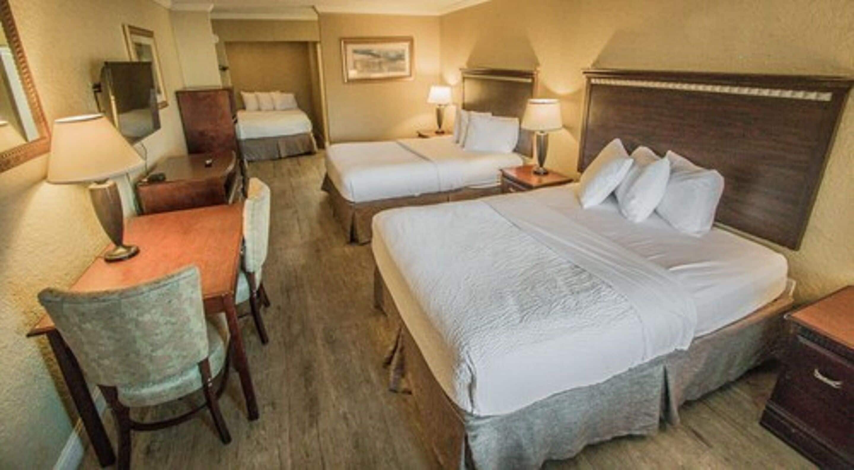 Quarto de hotel com duas camas, uma escrivaninha, uma cadeira e uma pequena mesa.