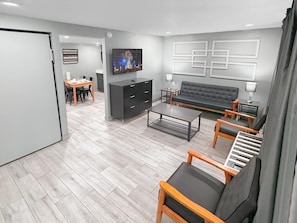 Uma sala de estar moderna com sofá, mesa de centro e televisão. Há também uma área de jantar com mesa e cadeiras.