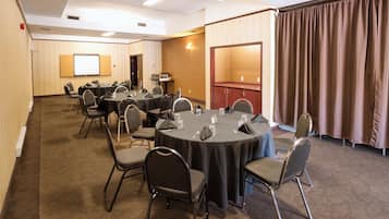 Uma sala de conferências com mesas redondas, cadeiras e uma tela de projeção.