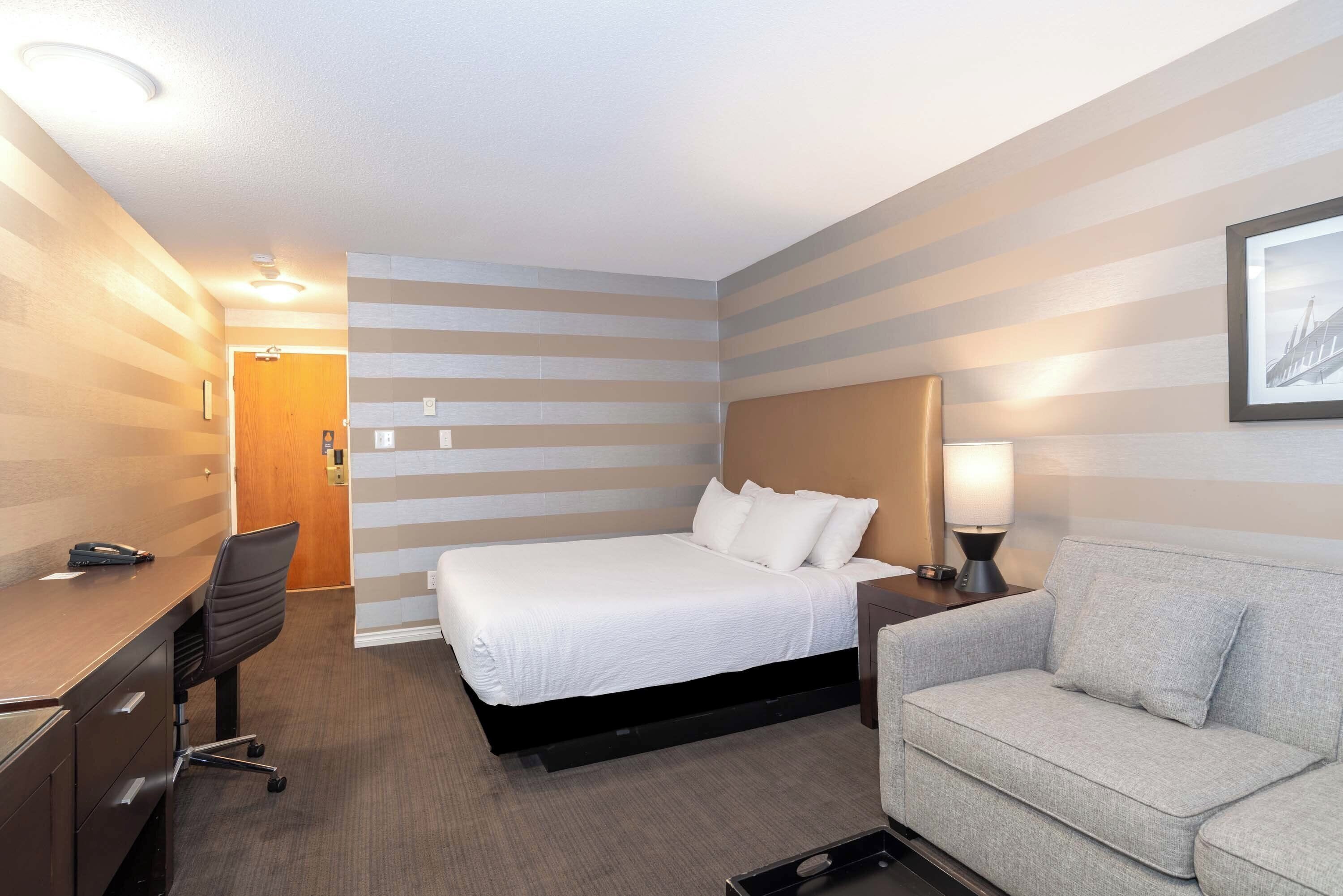 Quarto de hotel com cama, escrivaninha, poltrona, sofá e mesa de cabeceira com abajur.