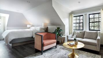Quarto de hotel moderno com cama, espreguiçadeira, sofá, mesa de centro e janelas amplas.