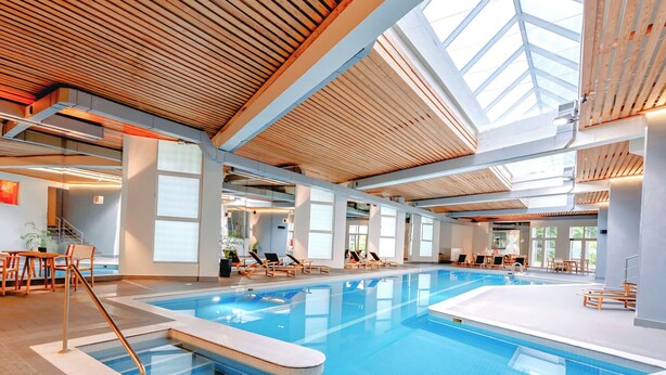 Piscina interna com água azul cristalina, deck de madeira e espreguiçadeiras.