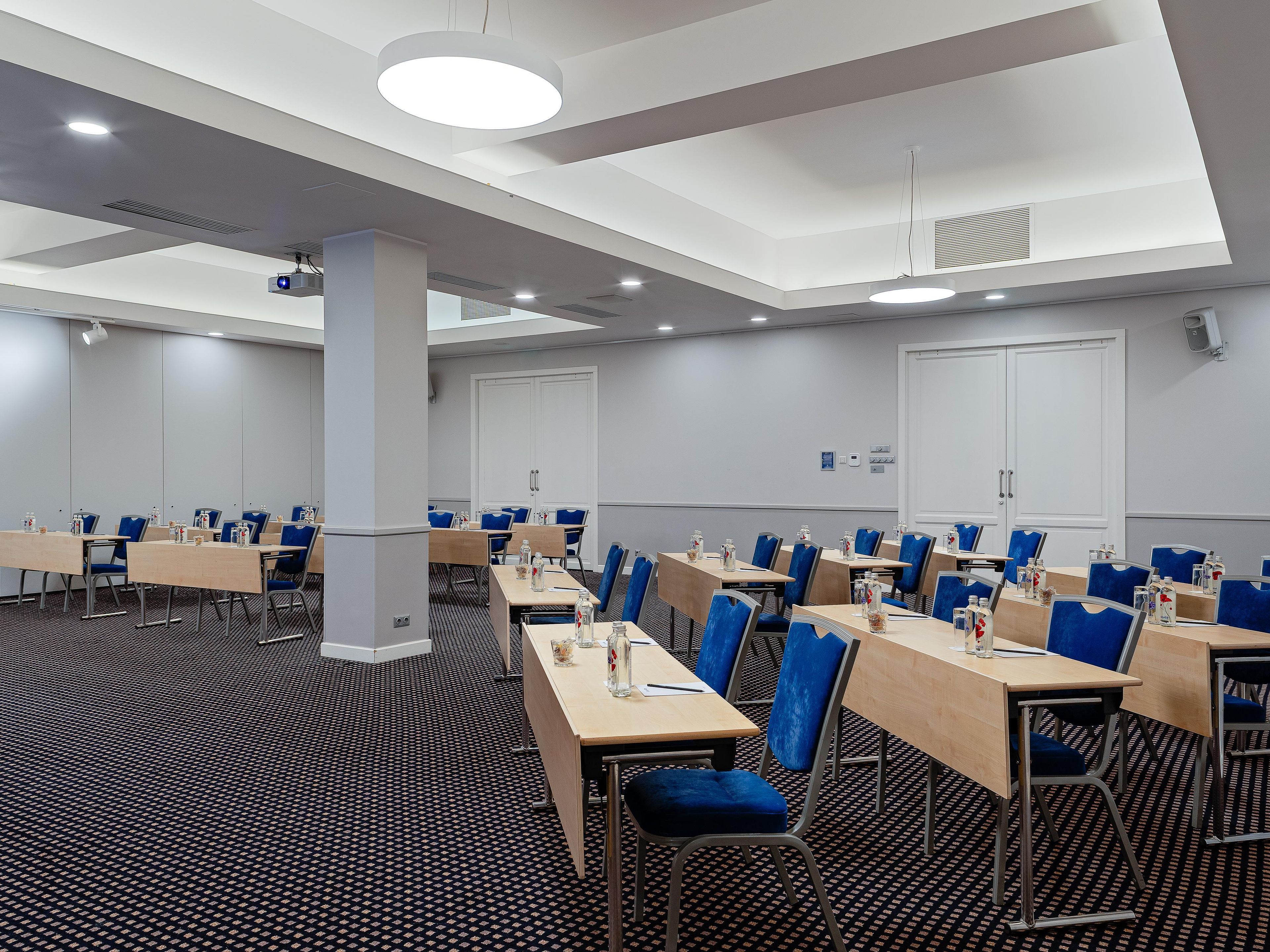 Sala de conferência com várias mesas e cadeiras, equipada com garrafas de água e placas de identificação.