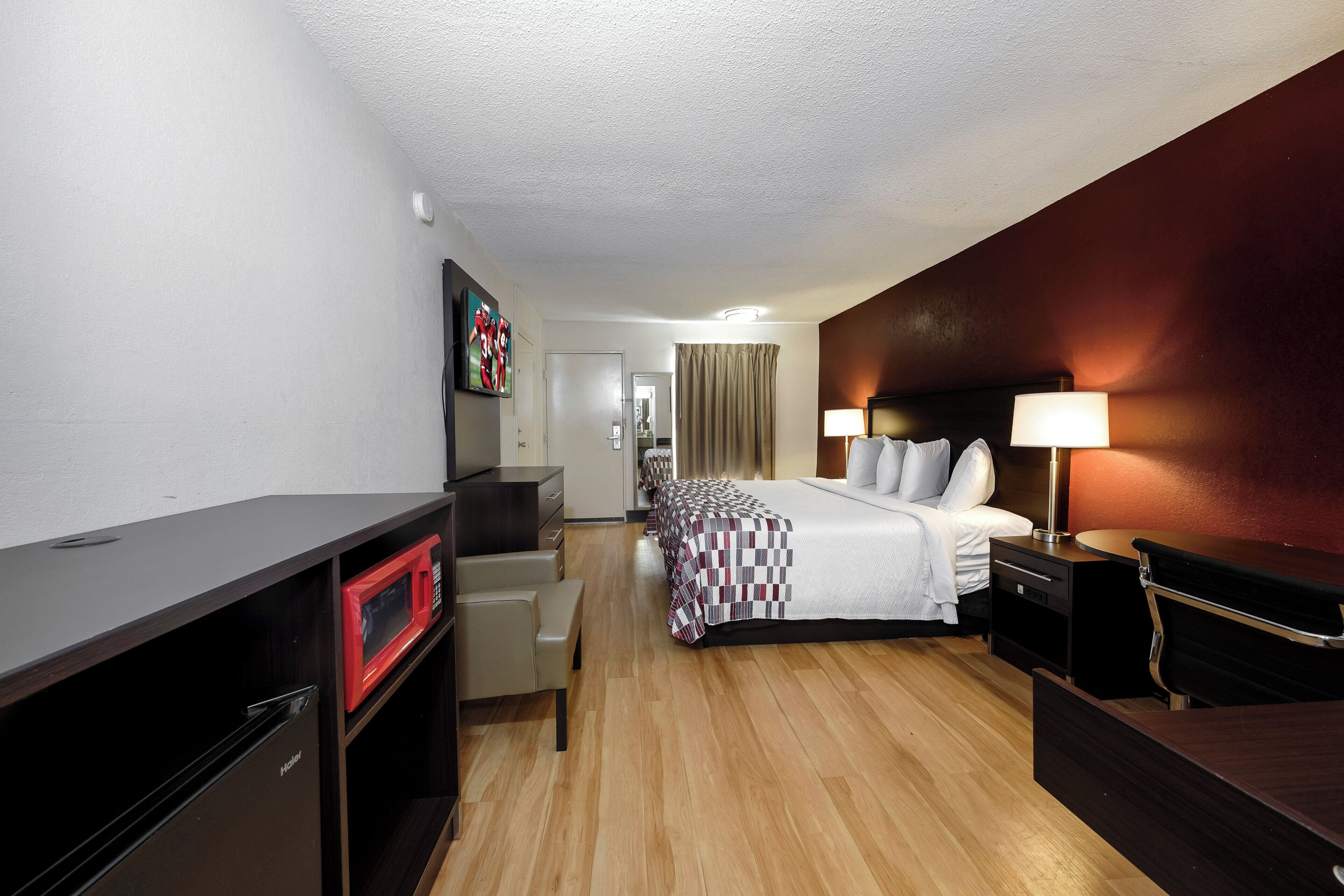 Quarto de hotel com uma cama, mesas de cabeceira, escrivaninha, televisão e micro-ondas.