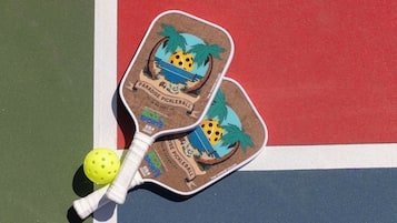 Duas raquetes de pickleball com design tropical em uma quadra.