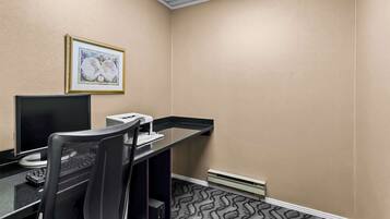 Quarto de hotel com escrivaninha, computador e quadro na parede.