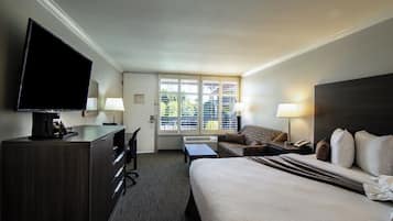 Quarto de hotel com cama, escrivaninha, televisão, sofá e janela com persianas.