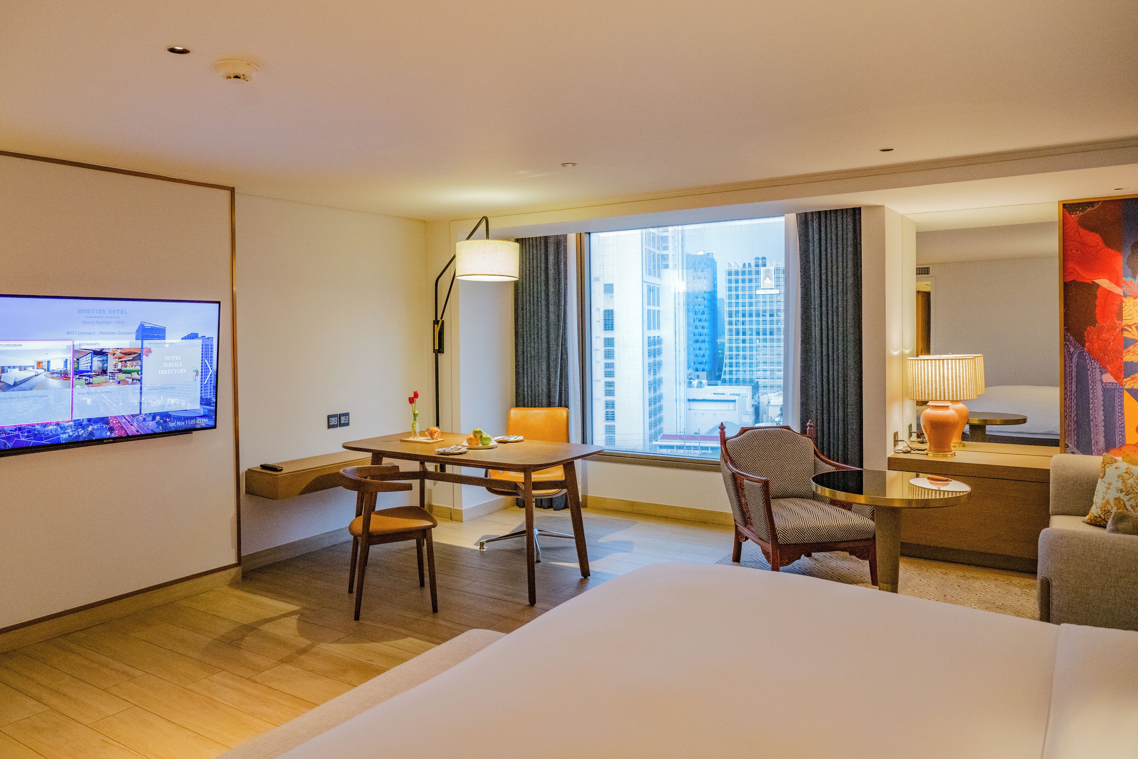 Quarto de hotel com uma cama, uma escrivaninha com cadeira, televisão na parede e uma janela grande com vista para a cidade.