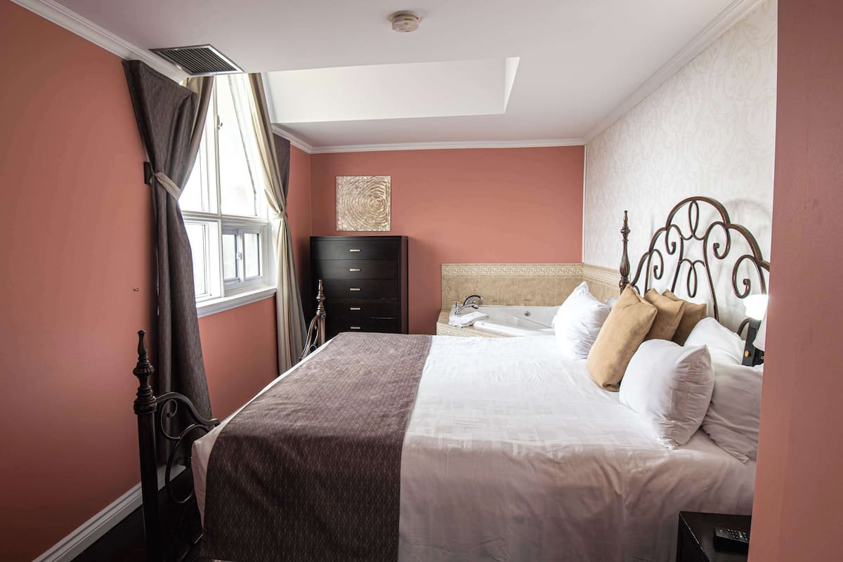 Quarto com cama, penteadeira, janela com cortinas e uma obra de arte na parede.