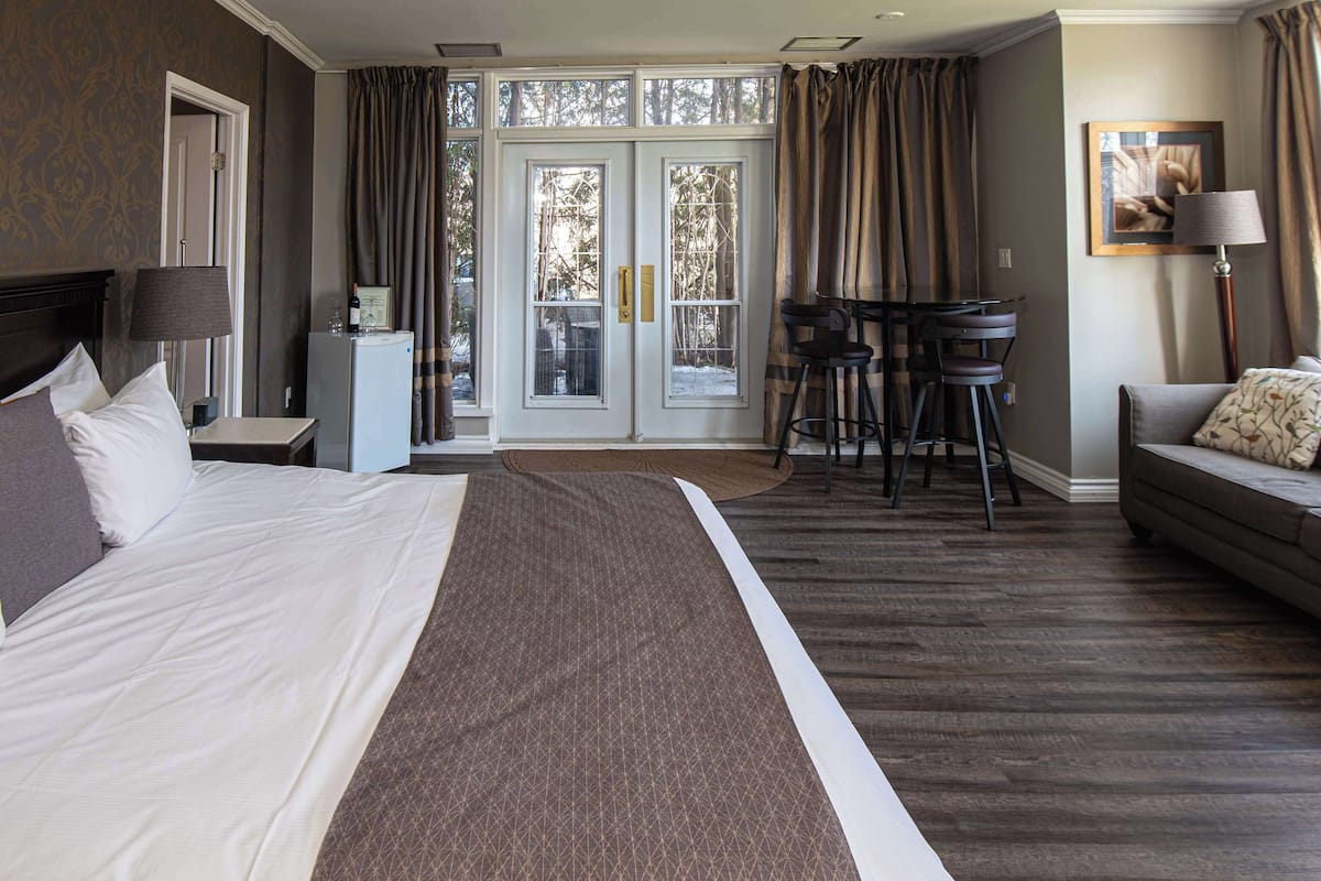 Quarto de hotel com uma cama grande, um sofá, área de refeições com cadeiras e vista por uma porta de vidro.