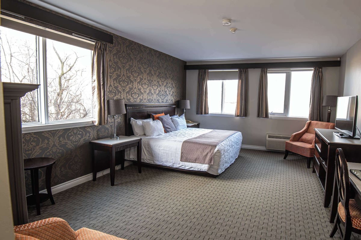 Quarto de hotel com uma cama grande, uma escrivaninha, uma cadeira e uma televisão.