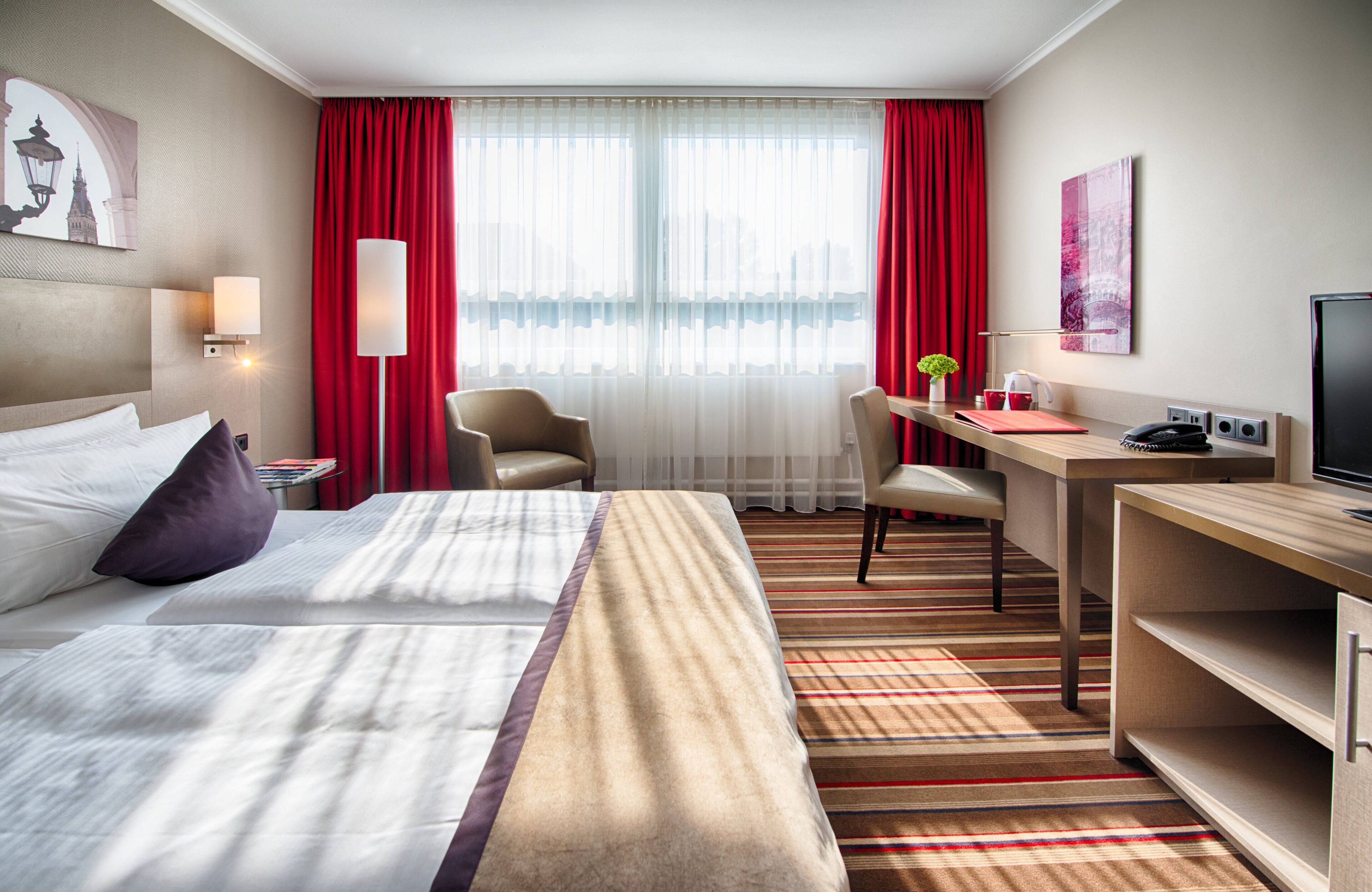 Quarto de hotel com duas camas, uma escrivaninha, uma cadeira, uma televisão e vista para a cidade.